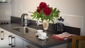 Uma bancada de cozinha com uma cafeteira, duas xícaras de café, um vaso com flores e um pano listrado em vermelho e branco.