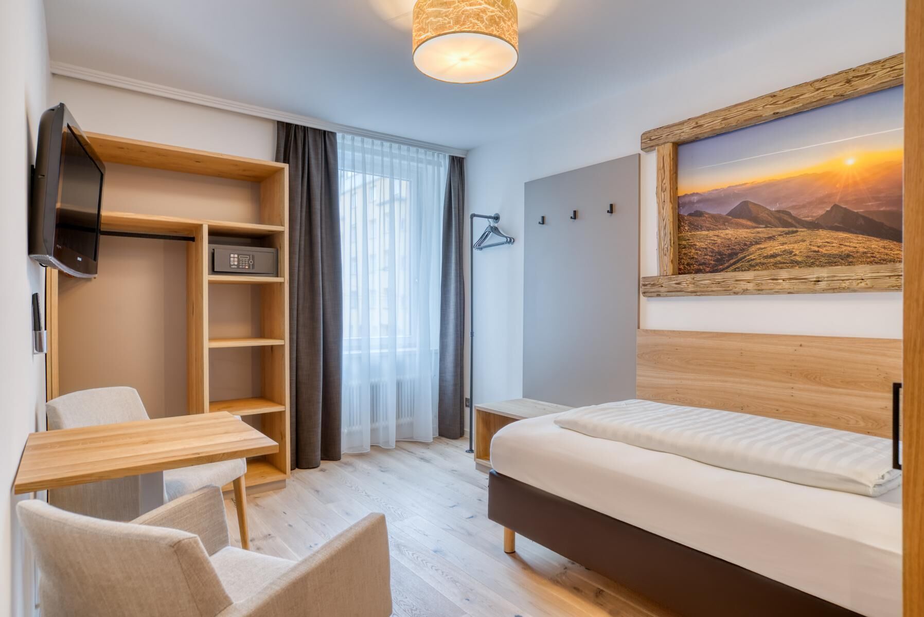 Quarto de hotel com cama, secretária, cadeira, televisão, guarda-roupa e um quadro na parede.