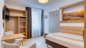 Quarto de hotel com cama, secretária, cadeira, televisão, guarda-roupa e um quadro na parede.