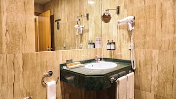 Uma casa de banho com parede de mármore, lavatório com espelho, porta-toalhas e secador de cabelo fixado na parede.