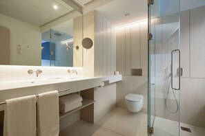 Uma casa de banho moderna com chuveiro envidraçado, um espelho grande e uma pia branca com duas torneiras.