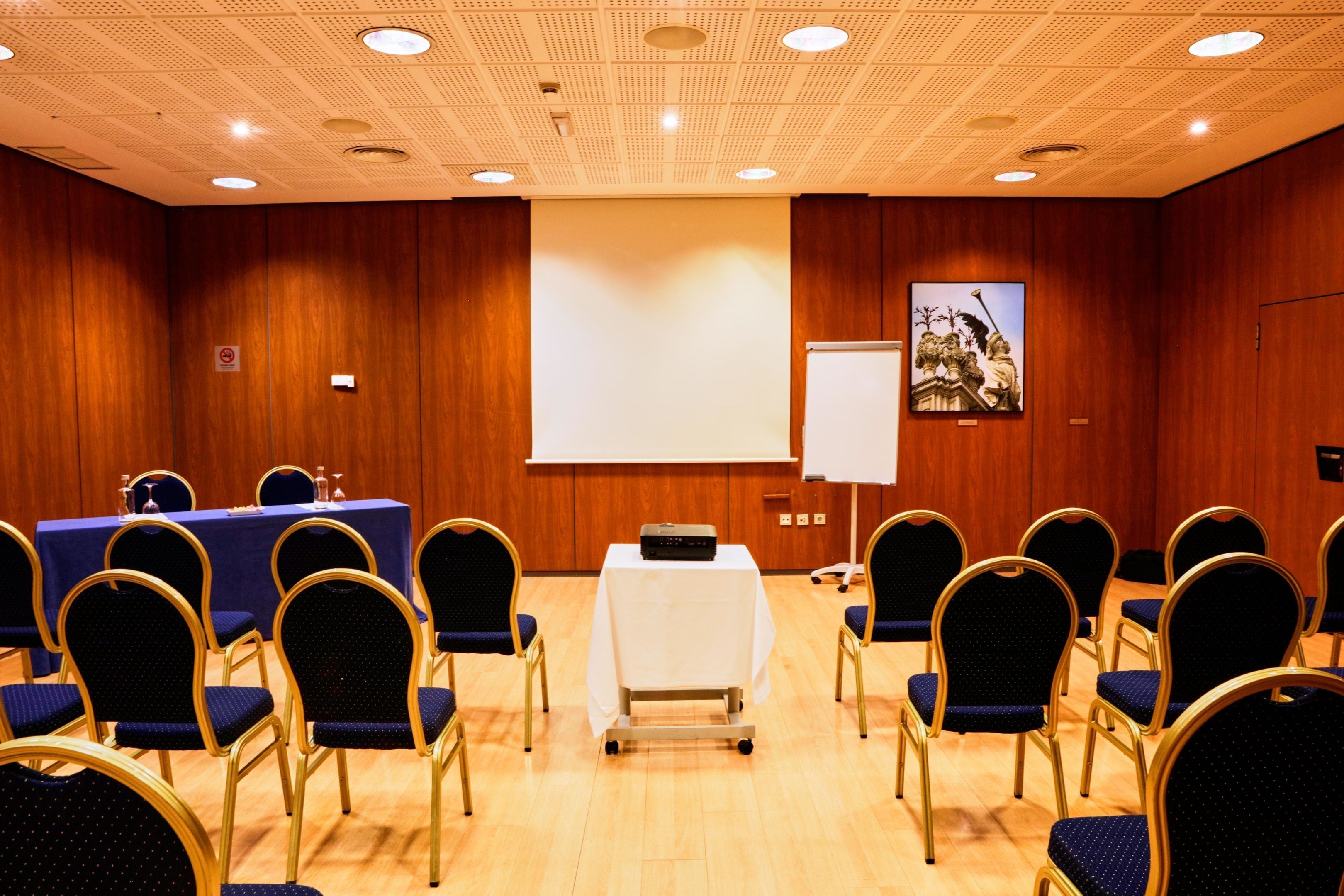 Uma sala de conferências com fileiras de cadeiras, um projetor sobre uma mesa e uma lousa.