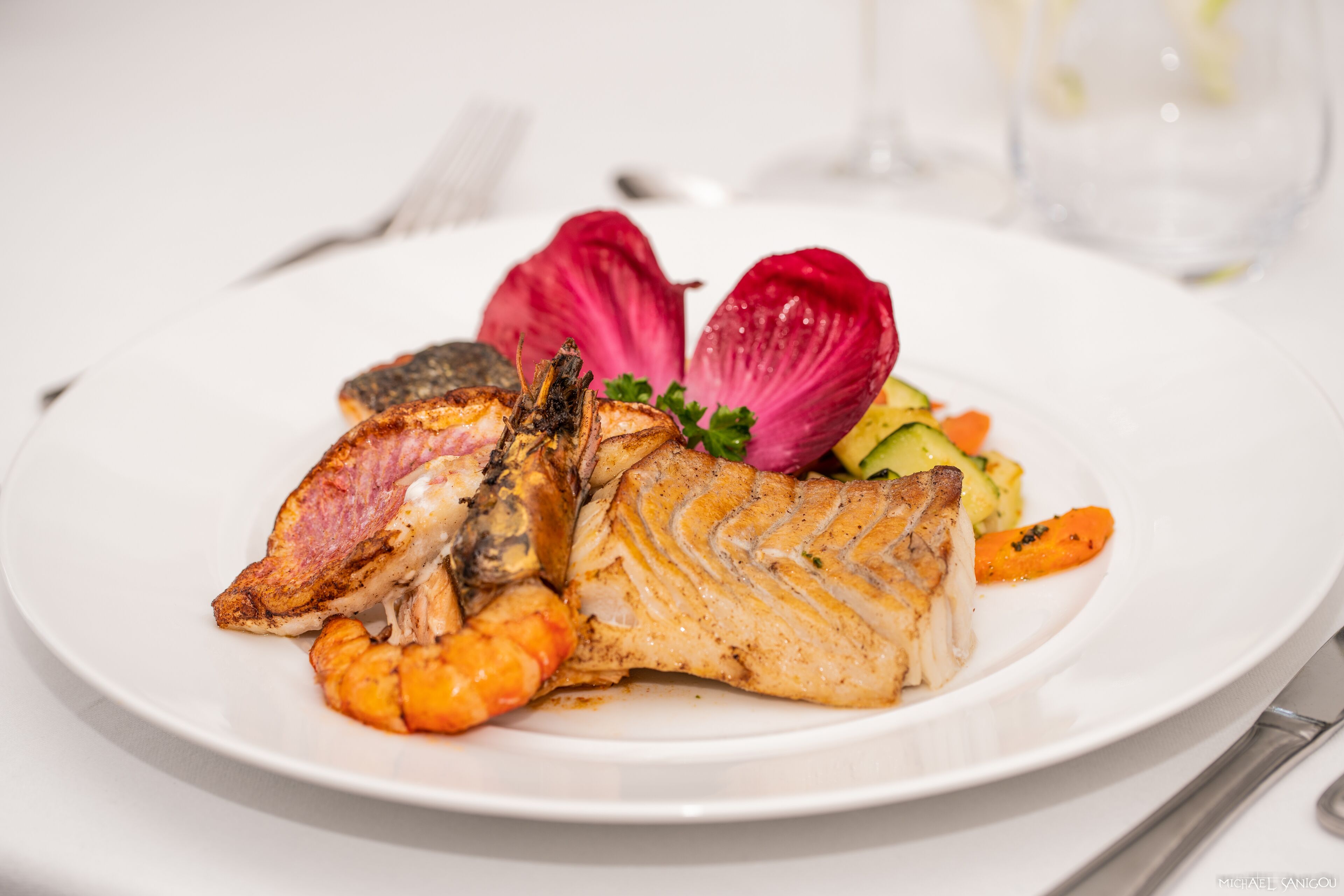 Prato com peixe grelhado, camarões e legumes.