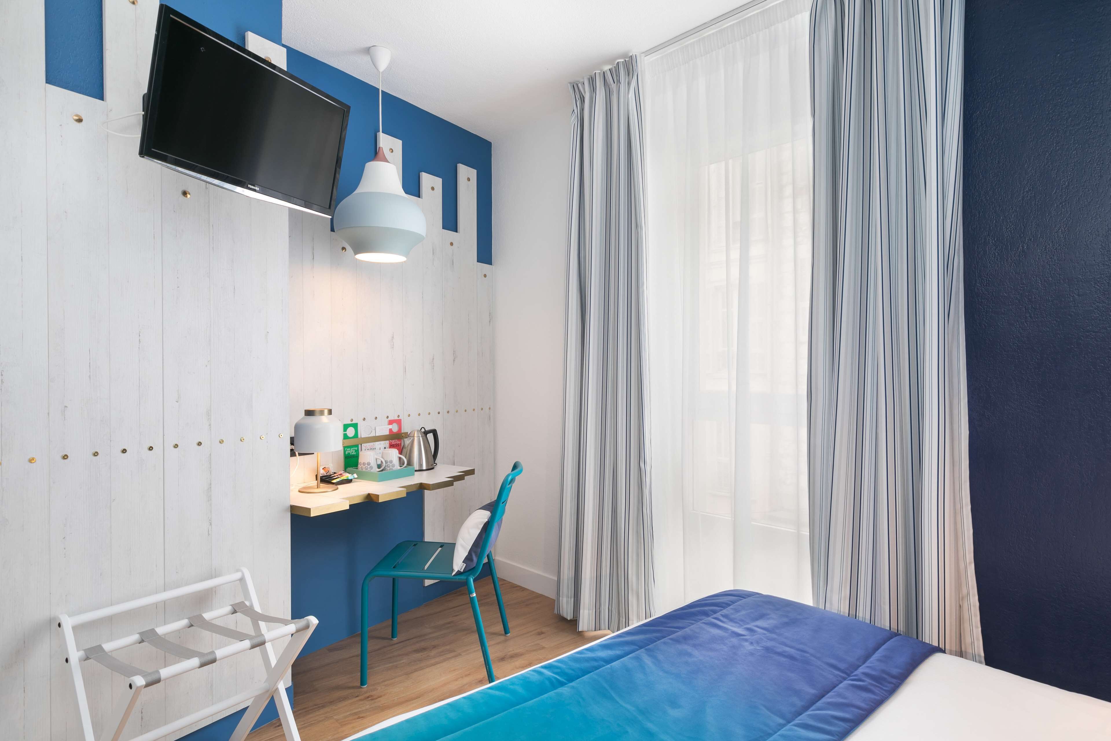 Quarto moderno com cama, escrivaninha, cadeira e TV fixada na parede.