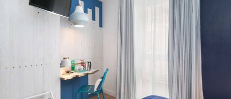 Quarto moderno com cama, escrivaninha, cadeira e TV fixada na parede.