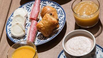 Uma mesa de madeira com uma bandeja de croissants, um copo de suco de laranja, uma tigela de cereais e uma xícara de café.