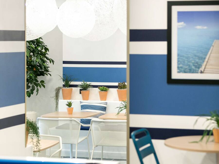 Uma mesa de bilhar em um ambiente com parede listrada em azul e branco, um quadro emoldurado e um vaso de planta.