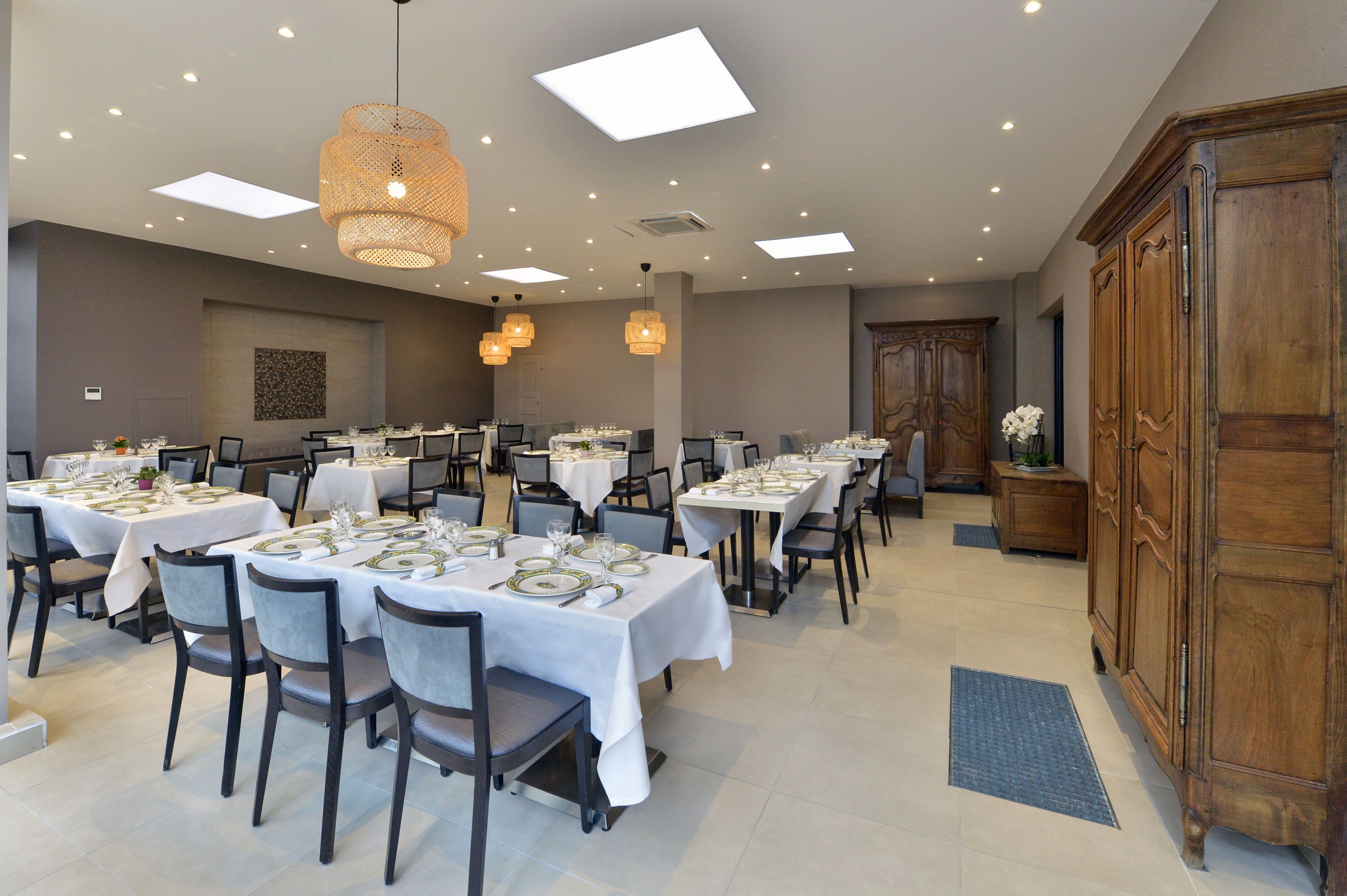 Uma sala de jantar com várias mesas preparadas para servir, com toalhas de mesa brancas e louças bem dispostas.