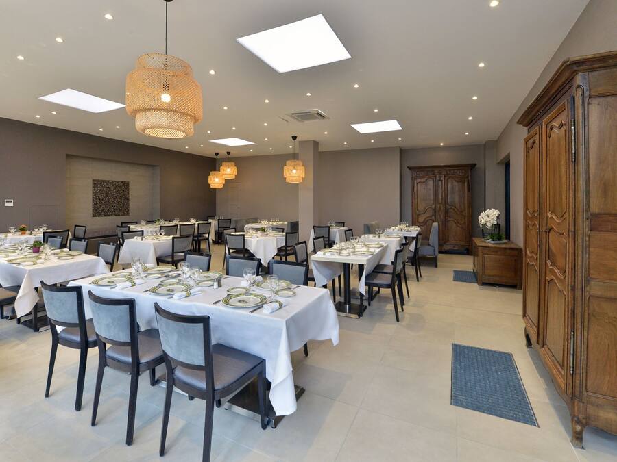 Uma sala de jantar com várias mesas preparadas para servir, com toalhas de mesa brancas e louças bem dispostas.