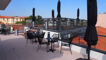 Terraço no telhado com área de estar externa, incluindo mesas e cadeiras, e vários guarda-sóis.