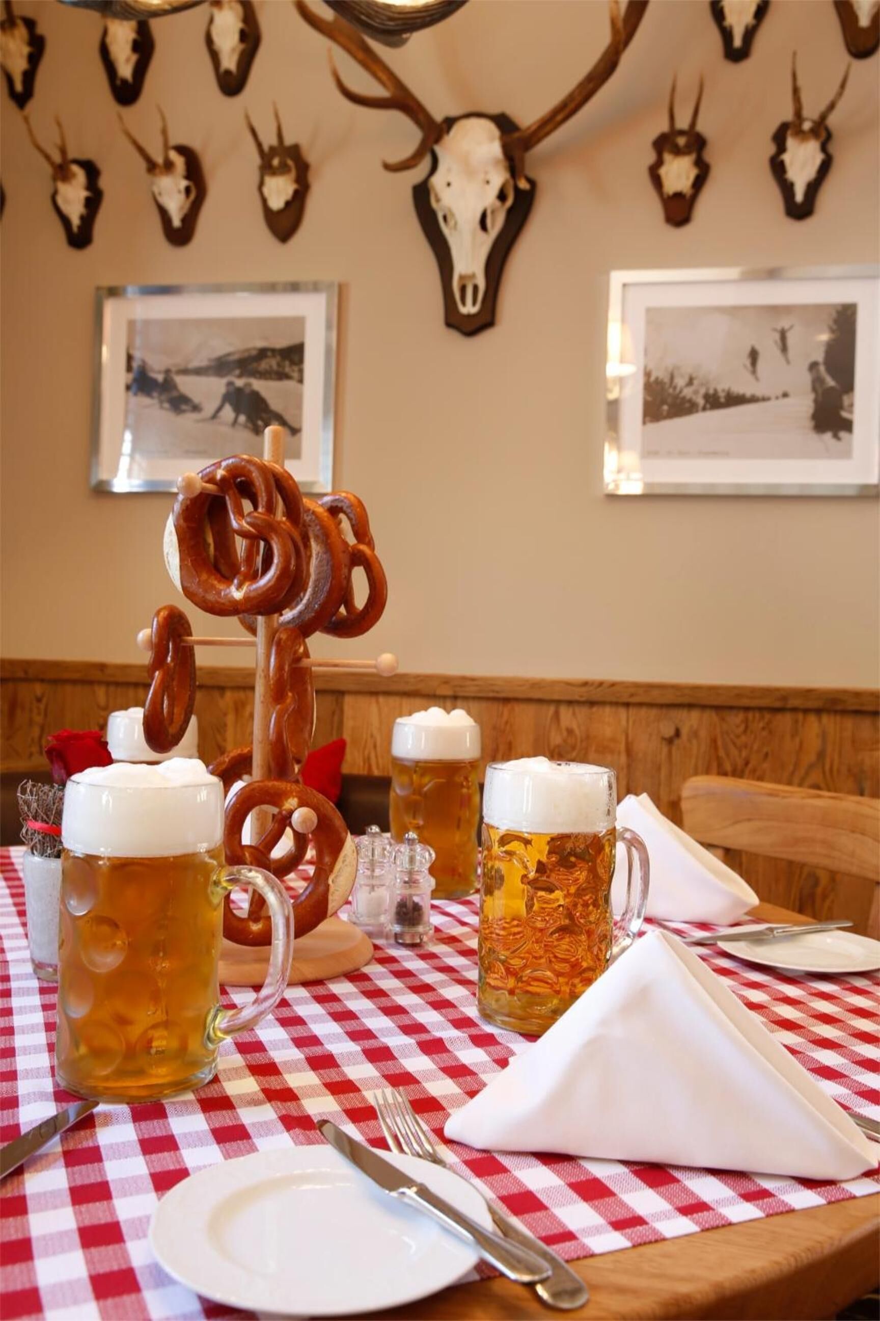 Uma mesa posta com canecas de cerveja, pretzels e um guardanapo branco sobre um tecido quadriculado.