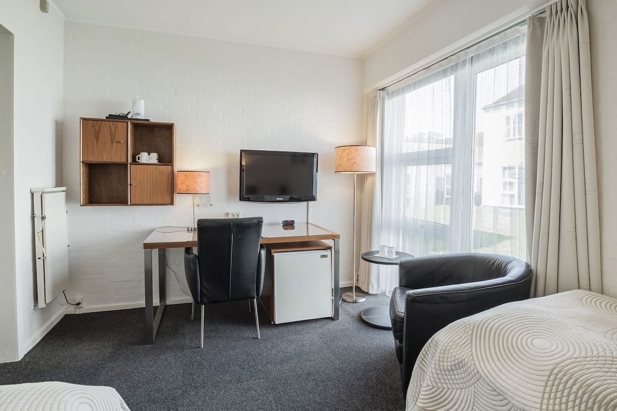 Quarto de hotel com escrivaninha, cadeira, televisão e cama.