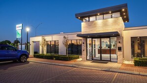 Entrada de hotel moderna com fachada de vidro, área de acesso coberta e placa indicando um hotel de conforto rural.
