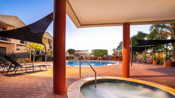 Uma área de piscina com espreguiçadeiras, uma banheira de hidromassagem e um espaço de estar coberto.