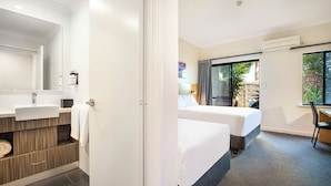 Quarto de hotel com banheiro, duas camas, uma escrivaninha e uma janela grande.
