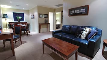 Uma sala de estar com um sofá de couro azul, uma mesa de centro de madeira e uma área de jantar com mesa e cadeiras.
