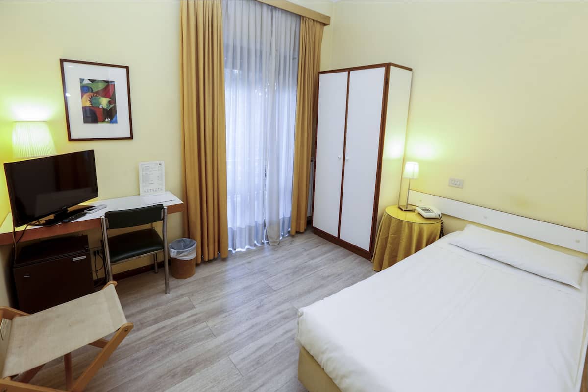 Quarto de hotel com cama, escrivaninha, cadeira, televisão e guarda-roupa.