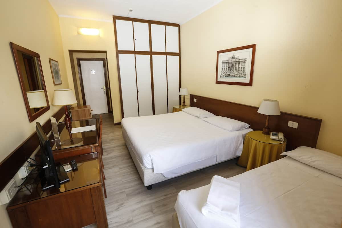 Quarto de hotel com duas camas, uma escrivaninha com computador, espelho, porta e luminária fixada na parede.