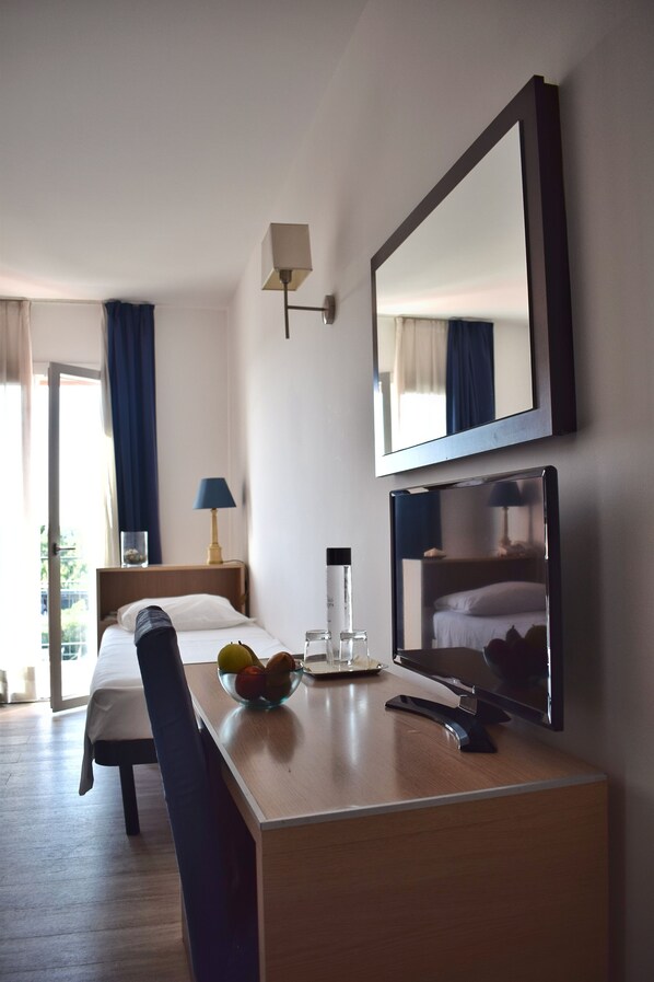 Quarto de hotel com uma cama, uma escrivaninha com uma tigela de frutas, uma luminária e um espelho grande.