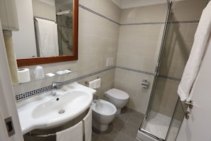 Casa de banho com lavatório, sanita, bidé e cabine de duche em vidro.