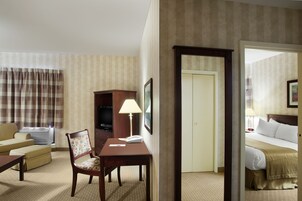Quarto de hotel com cama, escrivaninha, cadeira, televisão e abajur.