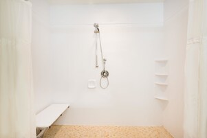 Um banheiro pequeno e branco, com chuveiro, saboneteira e prateleira.