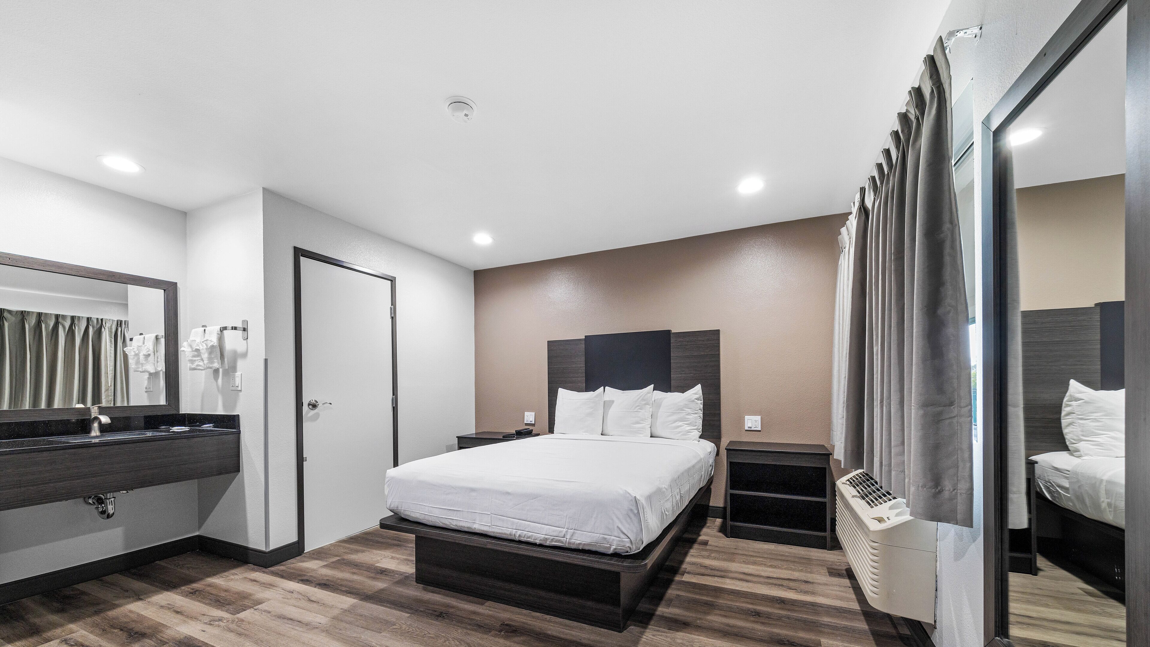 Quarto de hotel moderno com uma cama grande, banheiro com espelho e área de chuveiro.