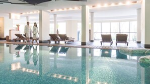 Piscina interior com espreguiçadeiras e um casal caminhando.