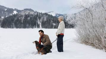 Paisagem nevada com uma pessoa ajoelhada ao lado de um cão e outra pessoa em pé nas proximidades.