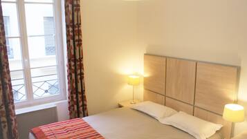 Quarto de hotel com cama, duas luminárias de cabeceira, janela com cortinas e vista para o exterior.
