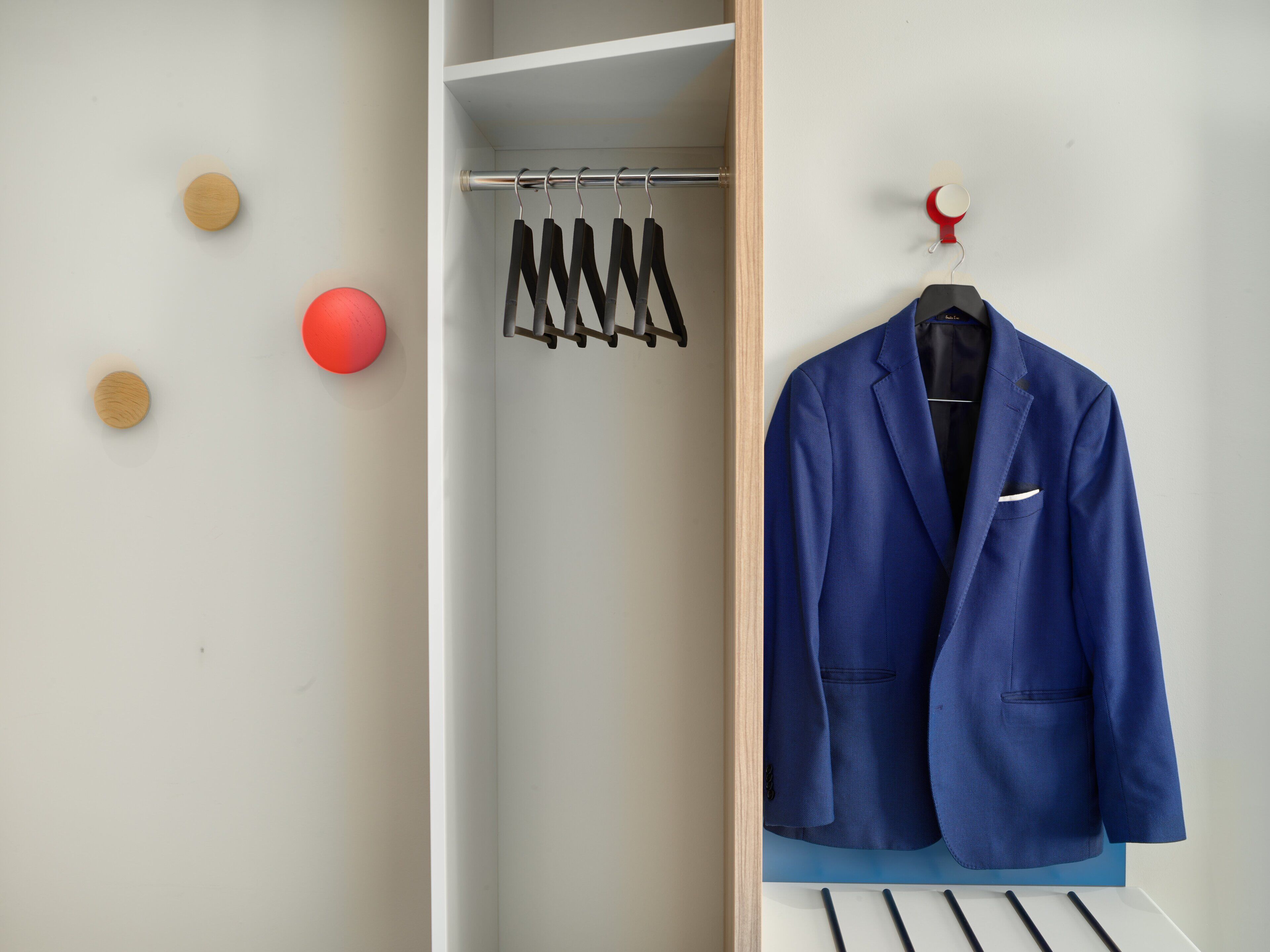 Um armário com um blazer azul pendurado em um cabide, uma bola vermelha e um objeto redondo de madeira na parede.