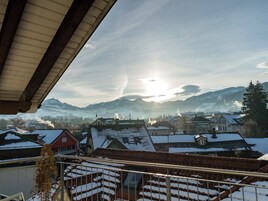 Vista de uma varanda com uma cidade coberta de neve e montanhas ao fundo.