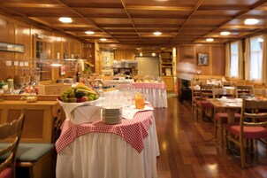 Uma sala de jantar com mesas preparadas para o café da manhã, com frutas e bebidas.