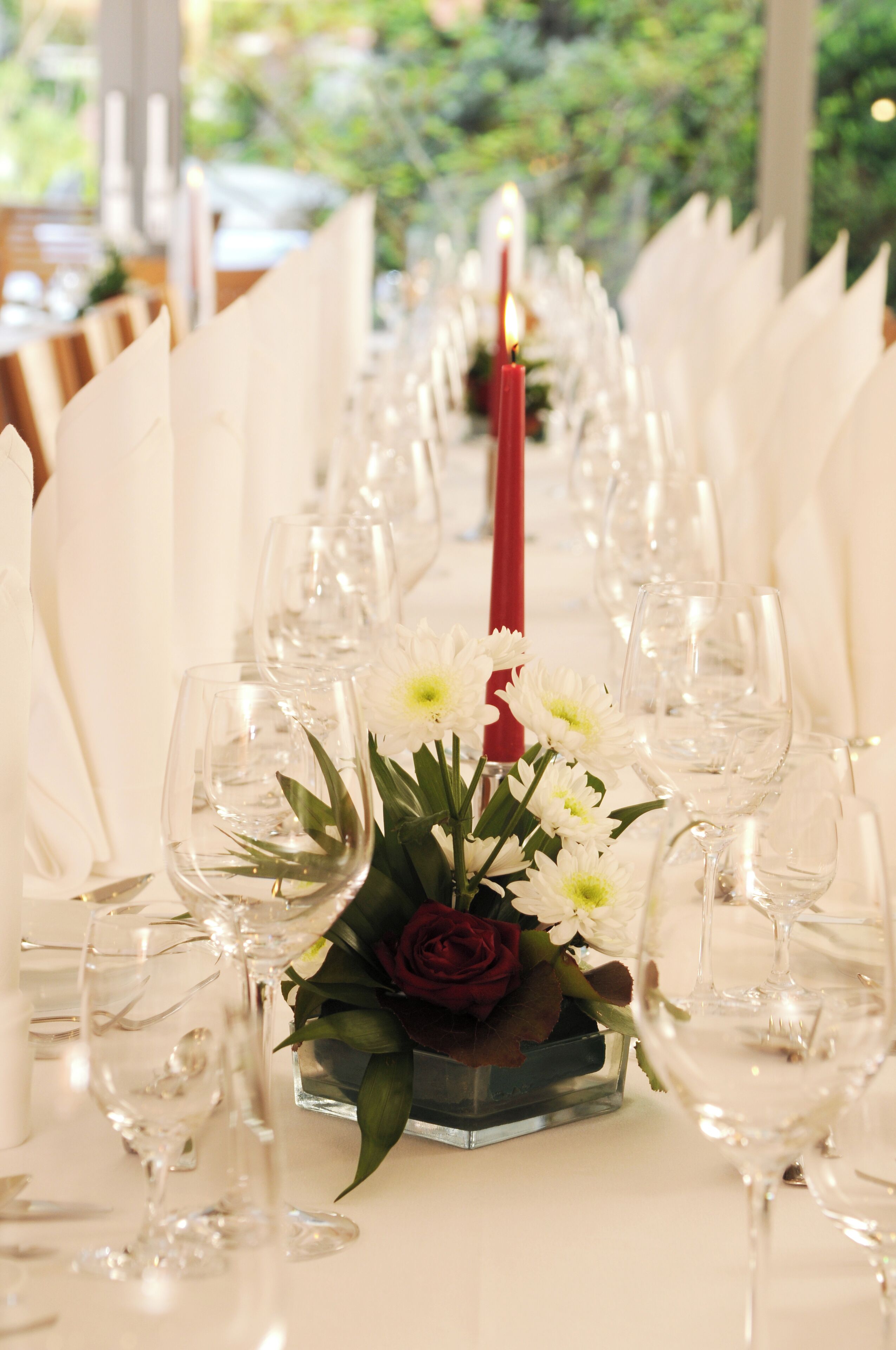 Uma mesa comprida posta para um evento formal, com copos transparentes e um arranjo floral central.