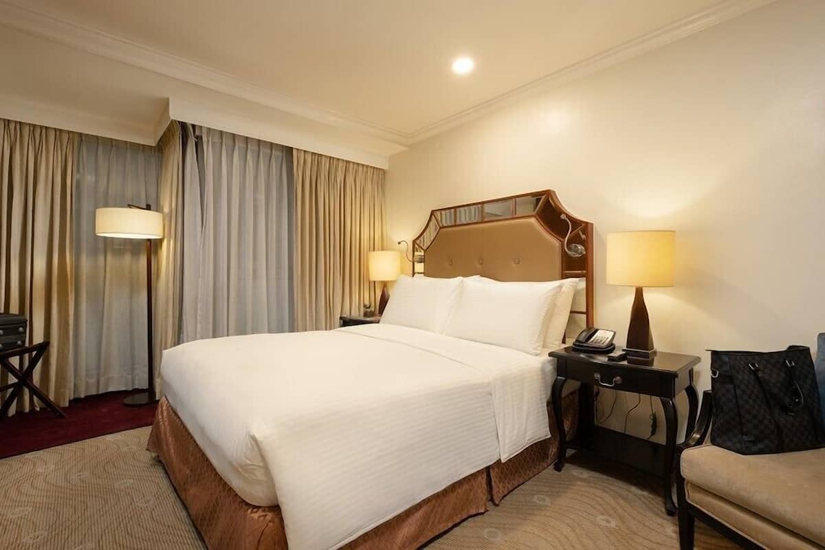 Quarto de hotel com uma cama grande, duas luminárias de cabeceira, uma escrivaninha com telefone e uma cadeira.