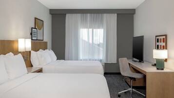 Quarto de hotel com duas camas, uma escrivaninha, uma cadeira, uma televisão e uma janela com cortinas.