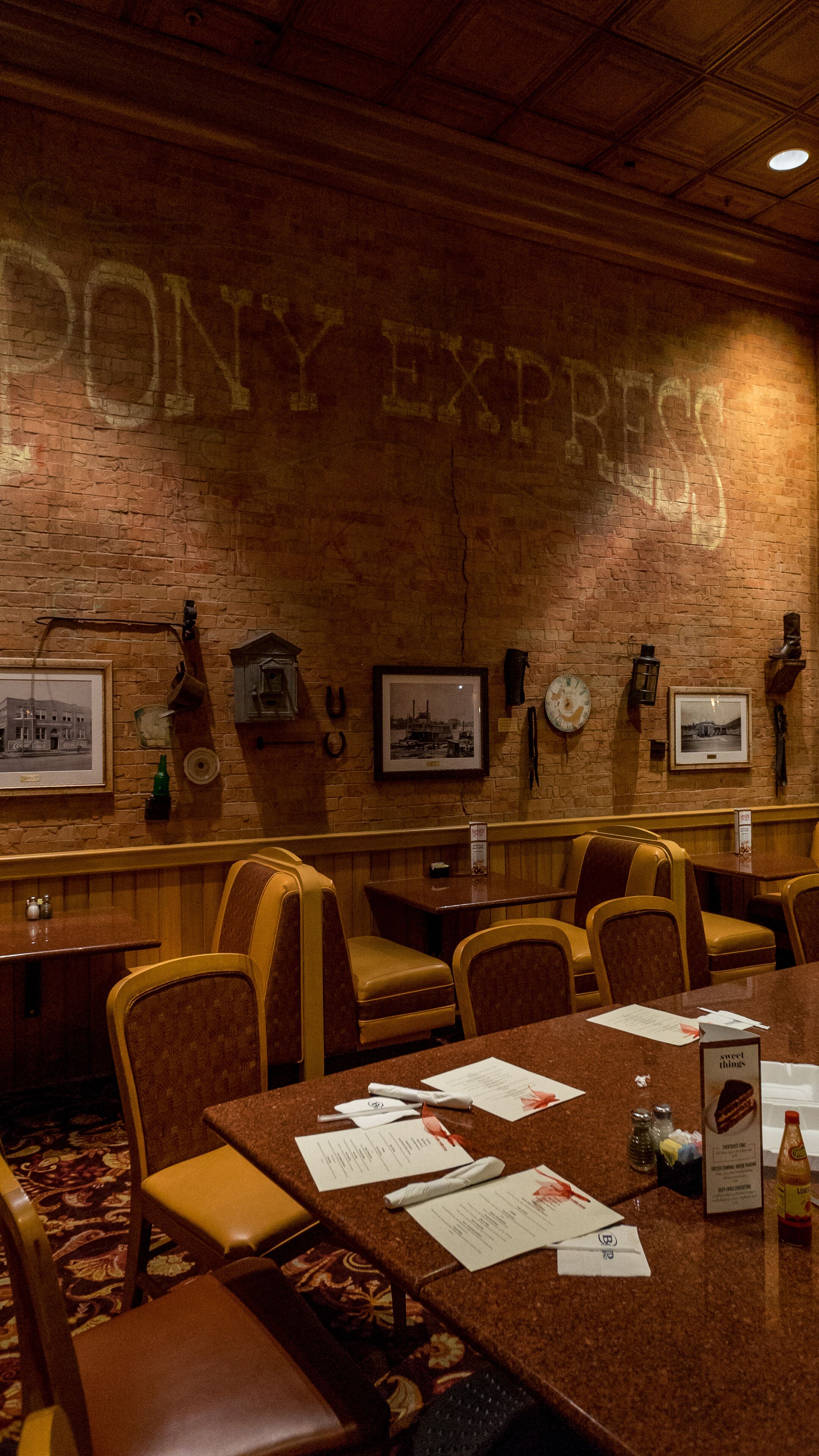 Um restaurante com parede de tijolos e decoração vintage, incluindo quadros e um letreiro de neon.