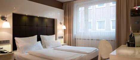 Quarto de hotel com uma cama de casal, uma escrivaninha com cadeira e uma janela com cortinas.