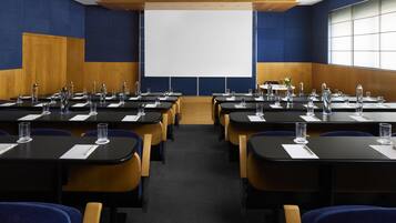 Uma sala de conferências com várias mesas, cadeiras e um grande ecrã.