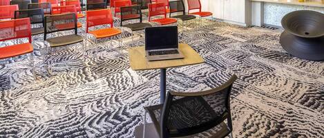 Uma sala de conferências com fileiras de cadeiras, um laptop sobre uma mesa e um tapete estampado.