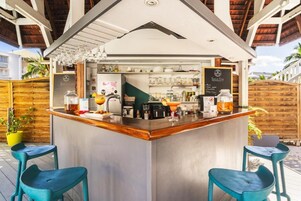 Uma área de bar ao ar livre com balcão, banquetas e um quadro de cardápio.