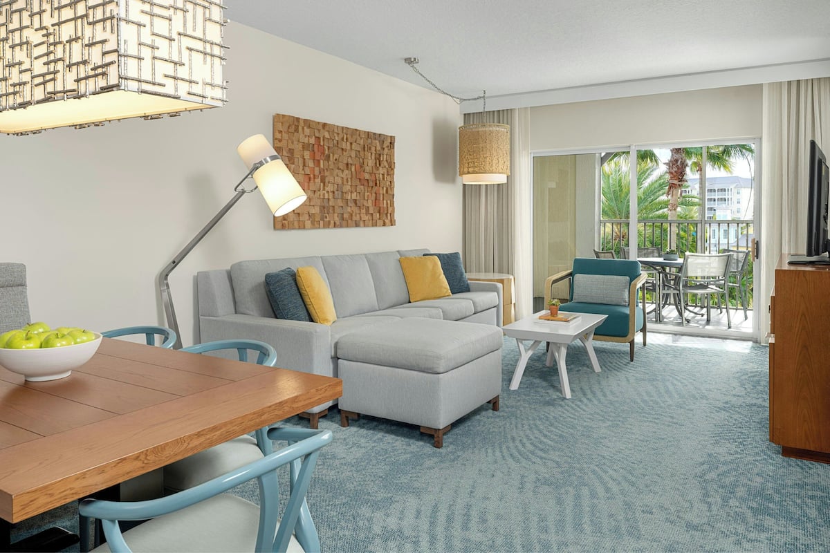 Uma sala de estar moderna com um sofá modular cinza, uma mesa de jantar de madeira e um tapete azul.