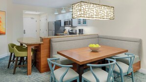 Uma cozinha moderna com ilha integrada, área de jantar com mesa de madeira e cadeiras azuis, e luminária pendente.