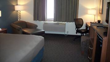 Quarto de hotel com cama, escrivaninha, cadeira, ar condicionado e janela com cortinas.