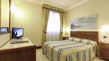 Quarto de hotel com cama, escrivaninha com computador, quadro na parede e janela com cortinas.