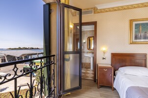 Quarto de hotel com varanda, cama, mesa de cabeceira, espelho e um quadro na parede.