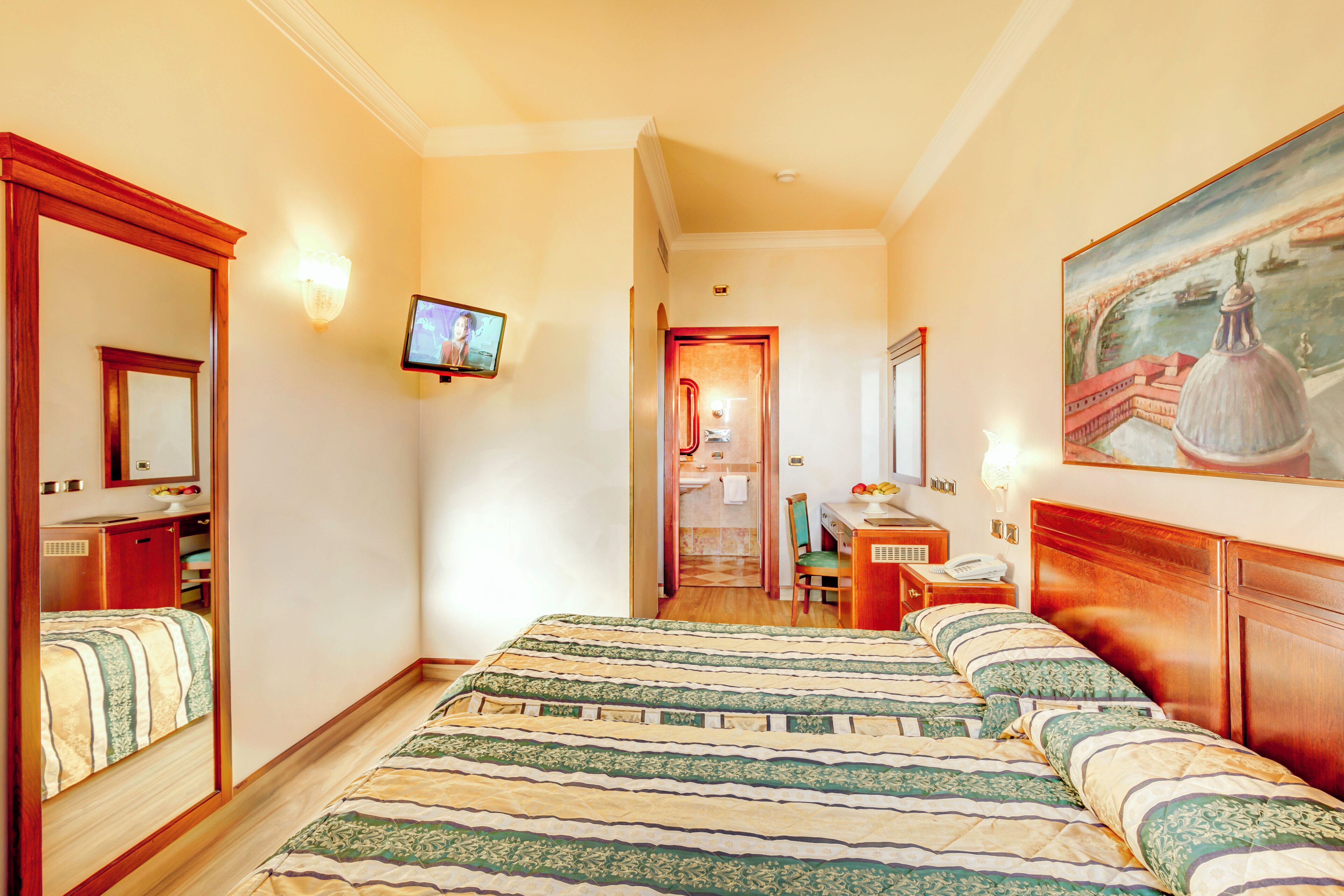 Quarto de hotel com uma cama grande, uma escrivaninha, uma cadeira, uma televisão e um quadro na parede.
