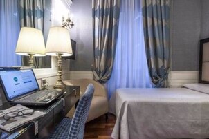 Quarto de hotel com escrivaninha, laptop e uma cama.