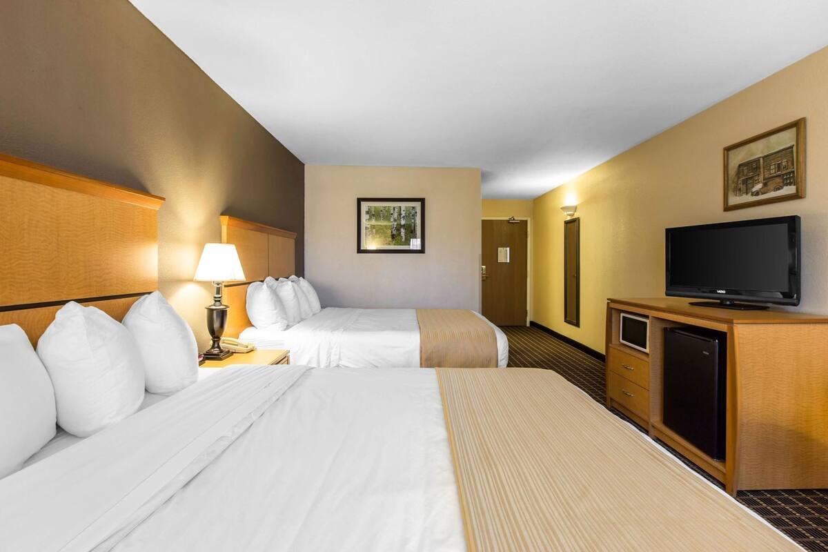 Quarto de hotel com duas camas, televisão, escrivaninha com abajur e frigorífico.