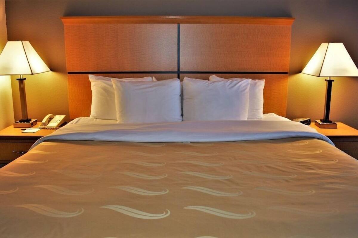 Quarto de hotel com uma cama grande, duas luminárias de cabeceira, mesa de cabeceira com telefone e cabeceira.
